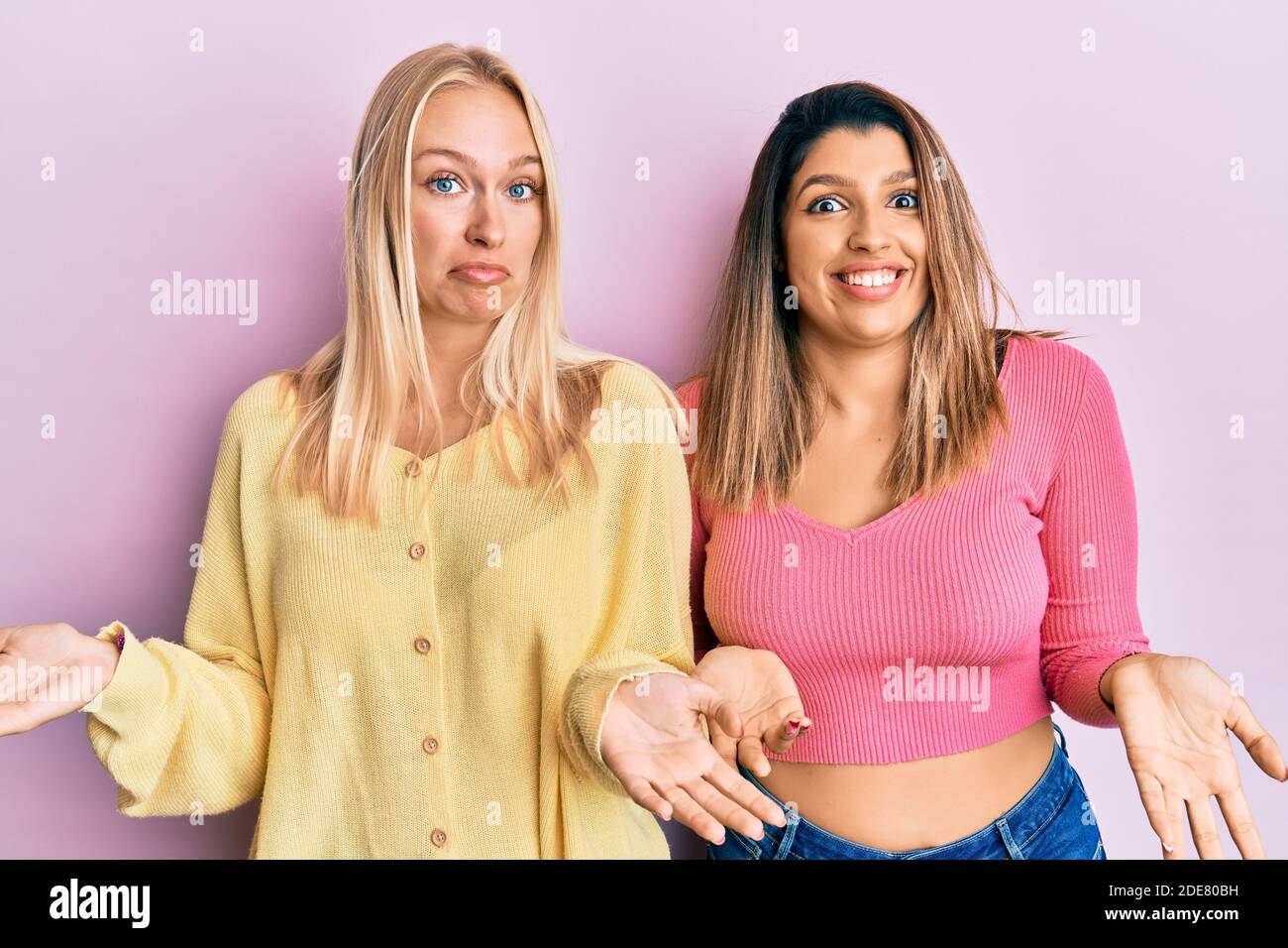 Two friends standing together over pink background clueless and ...