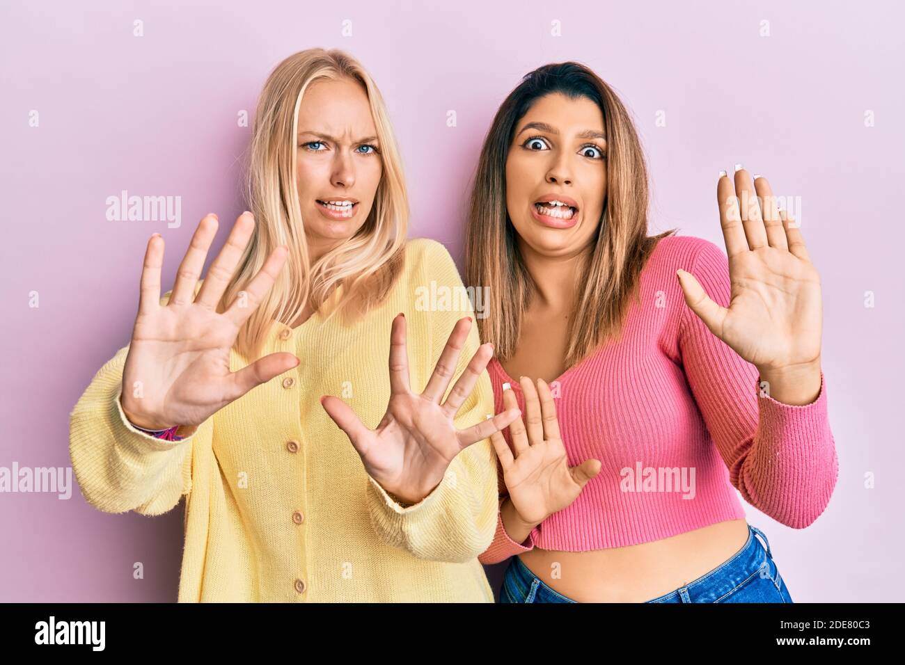 Two friends standing together over pink background afraid and terrified ...