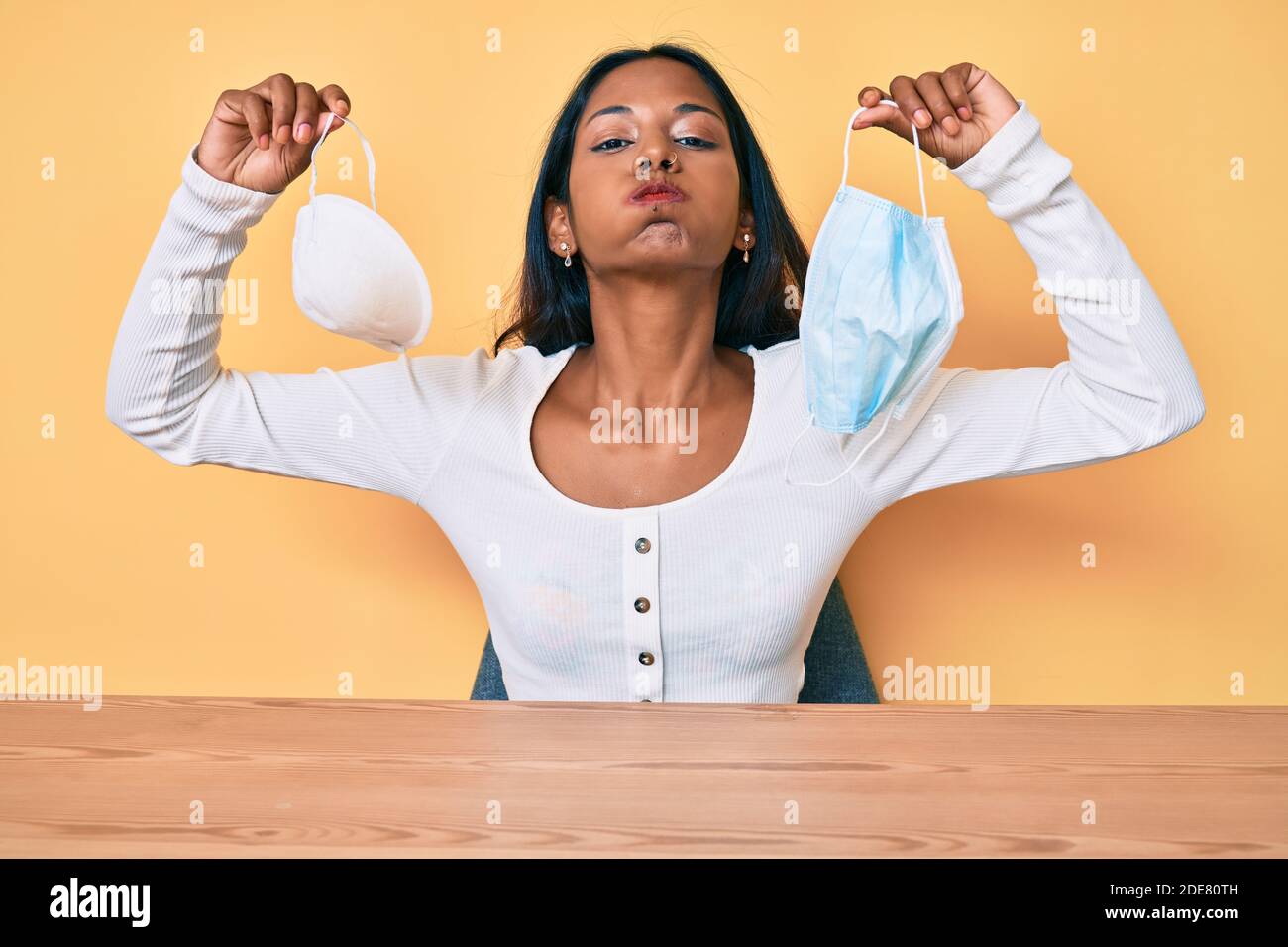 Young indian girl sitting on the table holding two diferent coronavirus ...