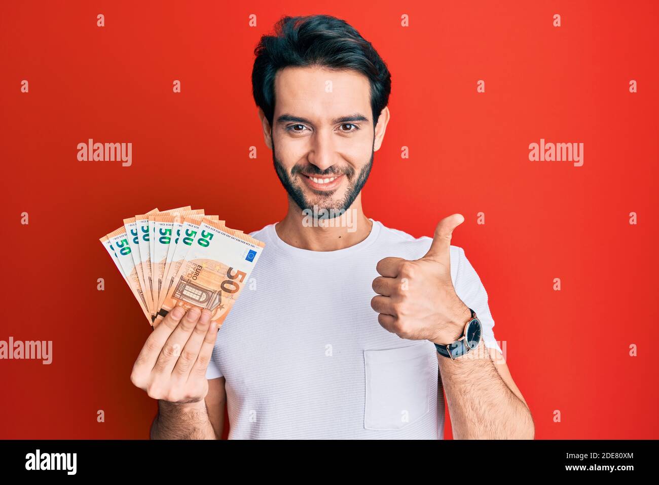 Young hispanic man holding euro banknotes smiling happy and positive ...