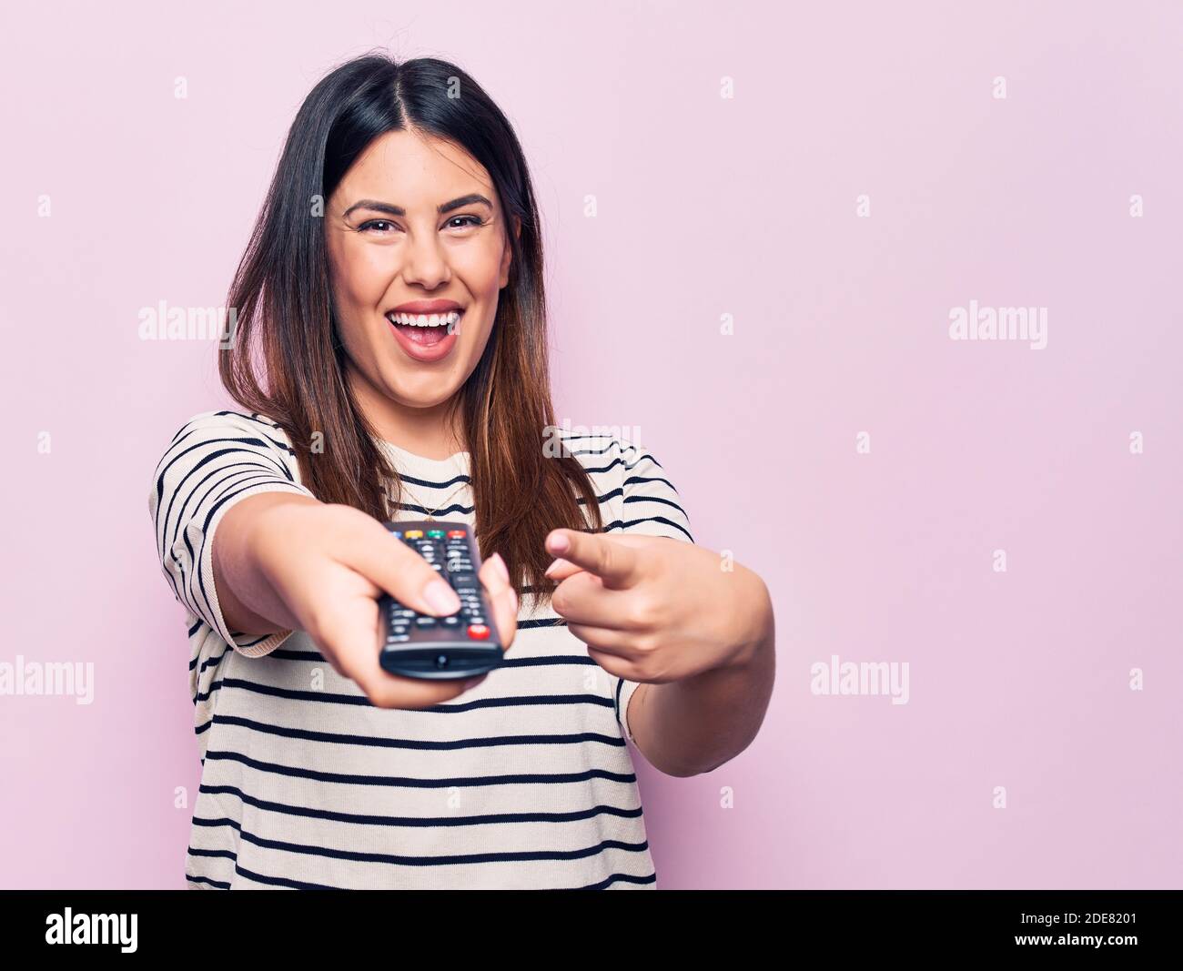 Young beautiful brunette woman holding television remote control over ...