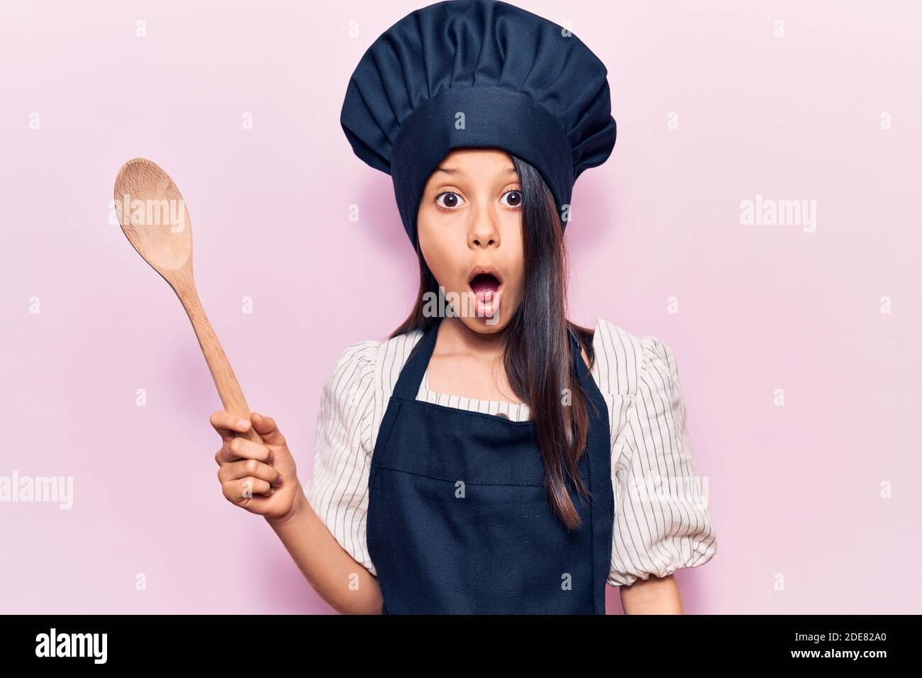 Beautiful child girl wearing cooker uniform scared and amazed with open ...