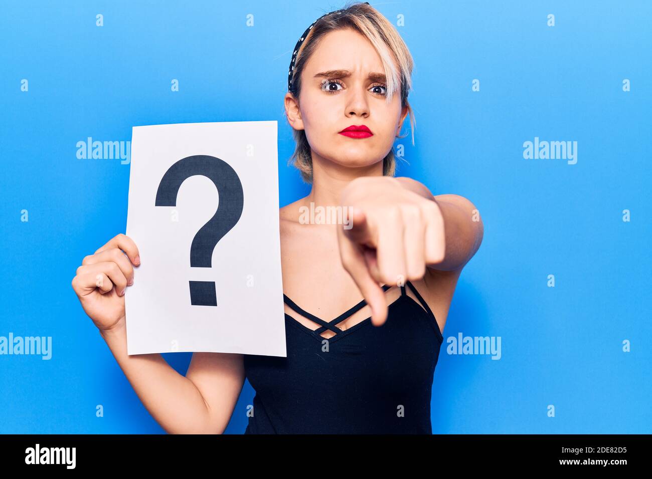 Young beautiful blonde woman holding question mark pointing with finger ...