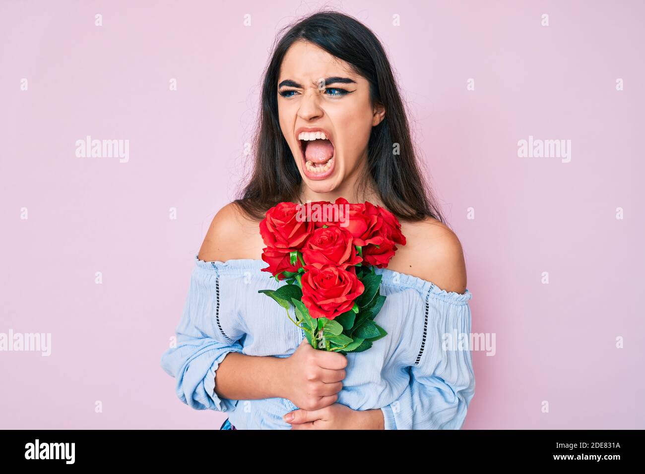 Brunette teenager girl holding flowers angry and mad screaming ...