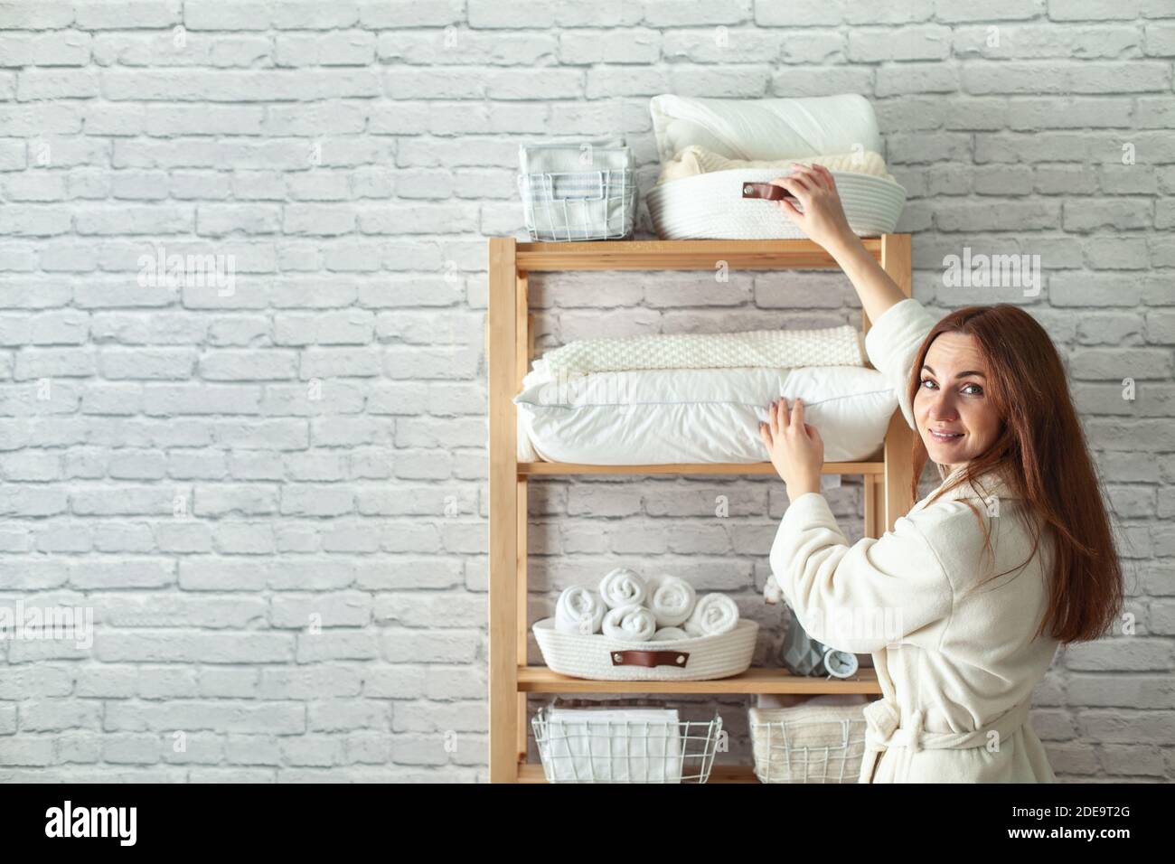 Young woman in warm robe is organizing linen closet with neatly folded ...