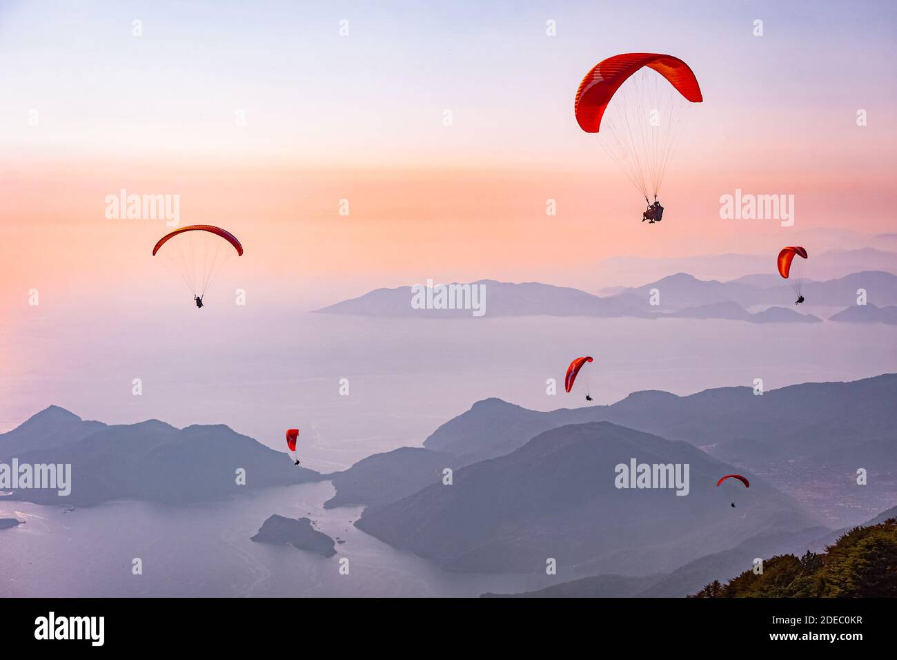 Paragliding in the sky. Paraglider tandem flying over the sea with mountains at sunset. Aerial ...
