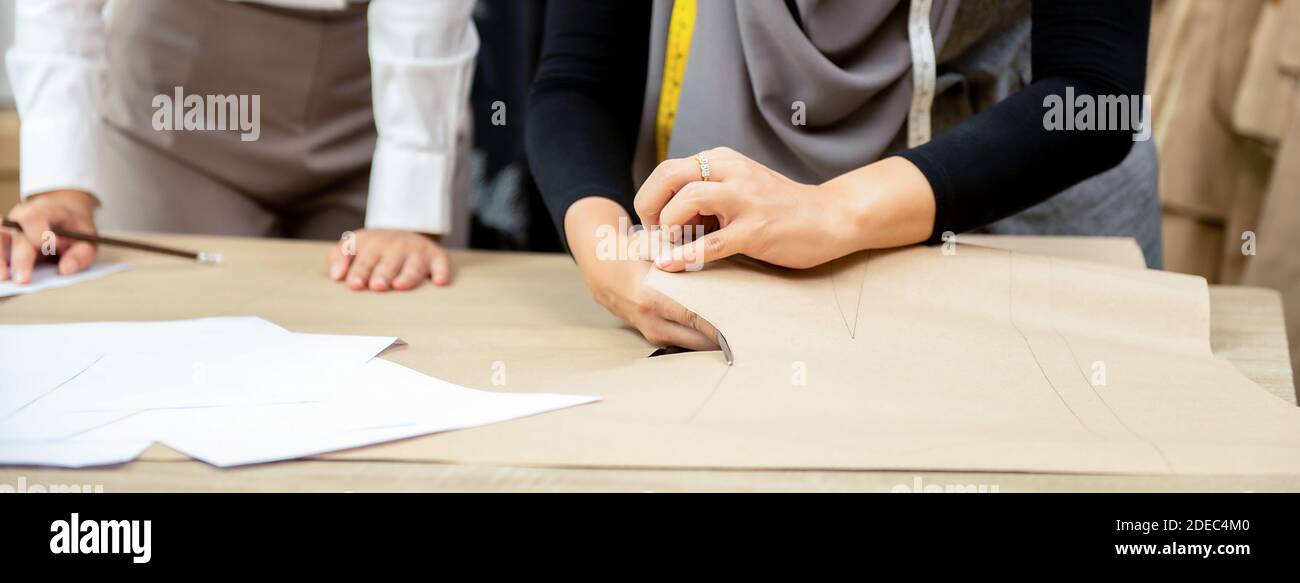 Muslim woman dressmaker cutting clothing pattern at the table in tailor ...