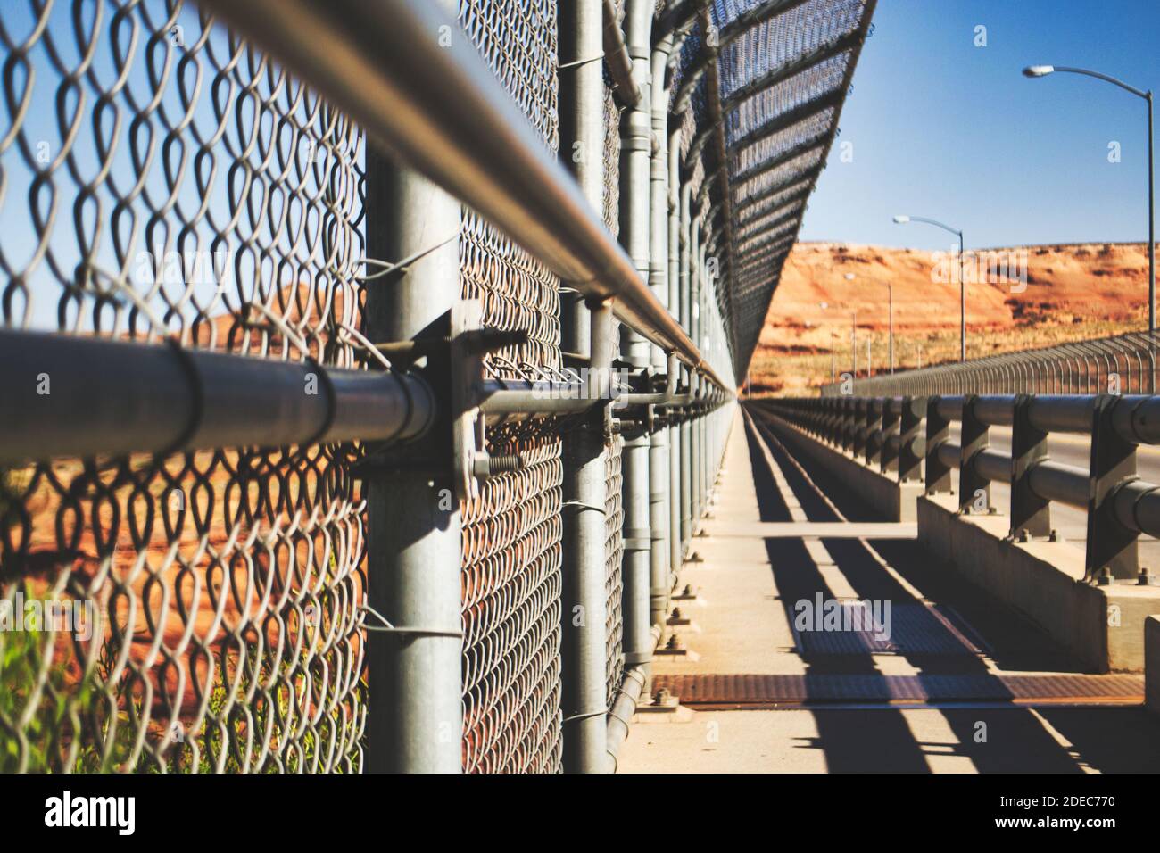 A narrow walkway on a bridge with chain-link fences under the sunlight ...