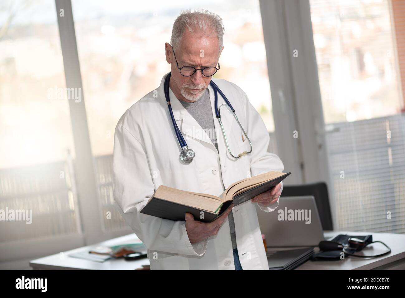 Senior doctor reading a textbook in clinic Stock Photo - Alamy