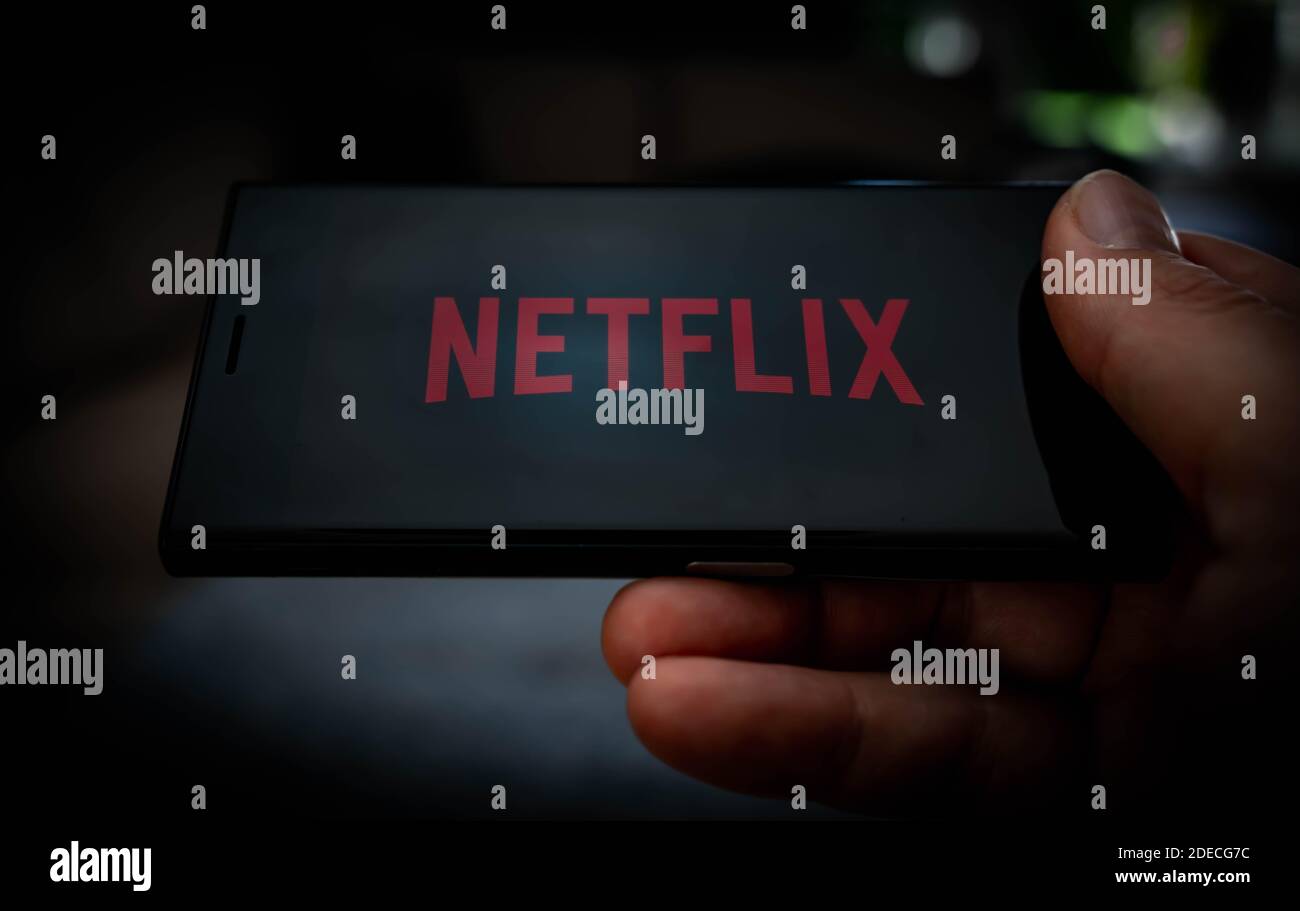 Hand holding a mobile phone with a Netflix logo displayed on the screen ...