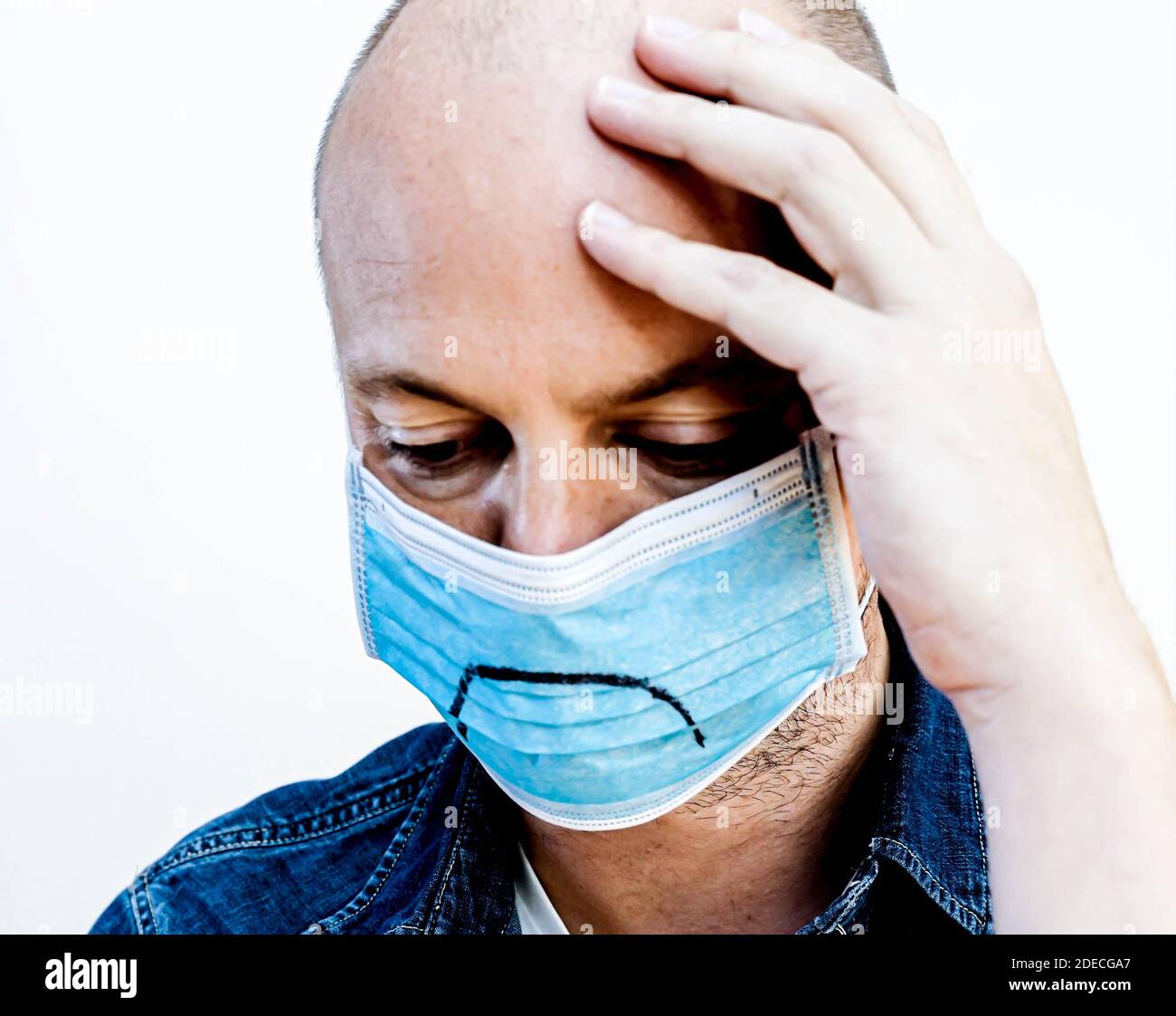 Man wearing a face mask with a sad smiley face, looking down in despair ...