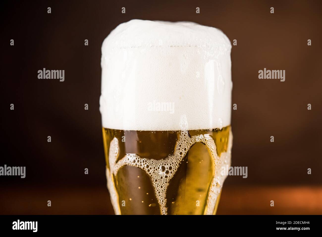 Golden cold beer in the glass on the table with overyflow frothy foam ...