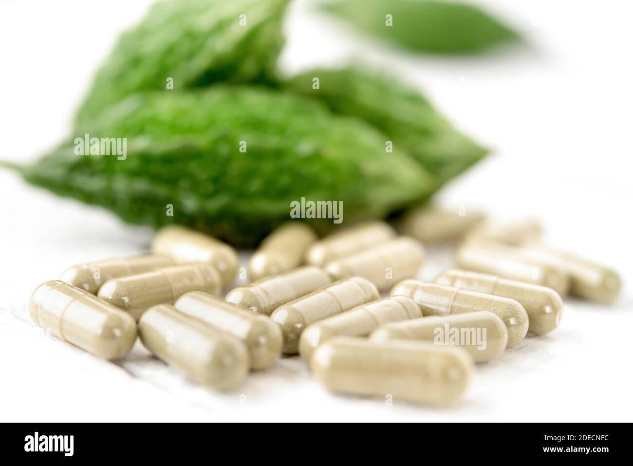 Green herbal extract capsules in front of bitter gourds against white ...