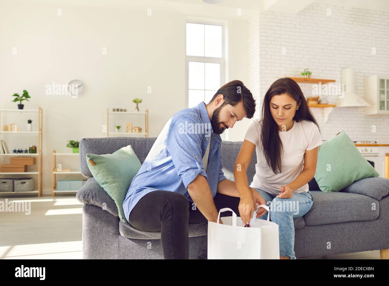 Young man and woman unpack a white bag of groceries delivered to them ...
