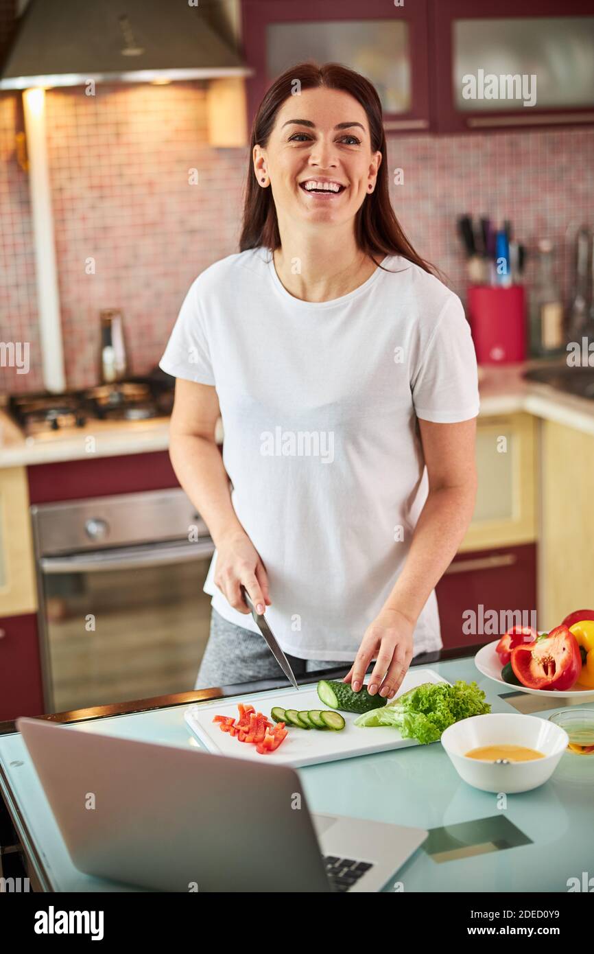 Laughing housewife getting distracted from cutting salad components ...
