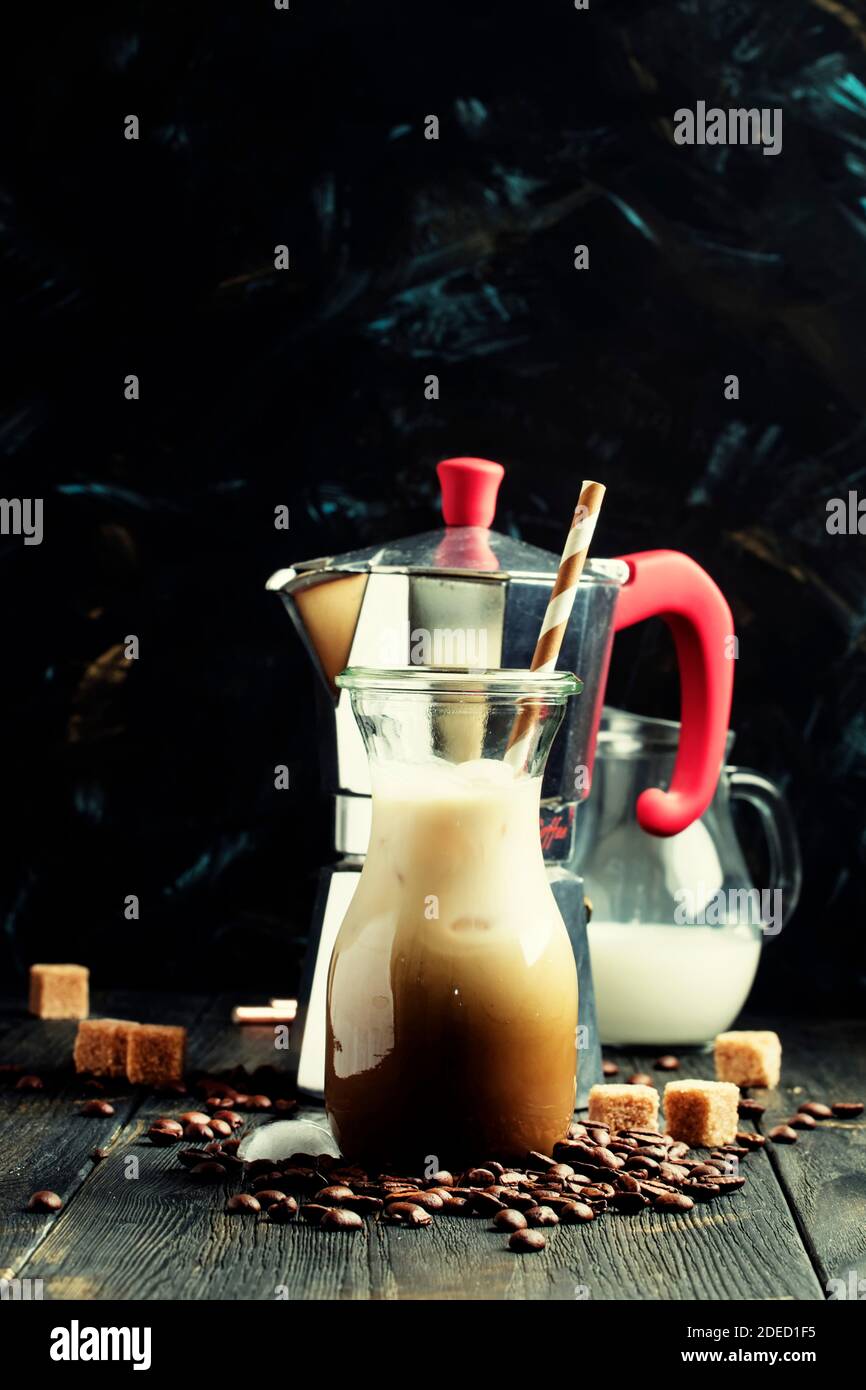 Cold iced coffee with milk and ice in a glass jug, dark background ...