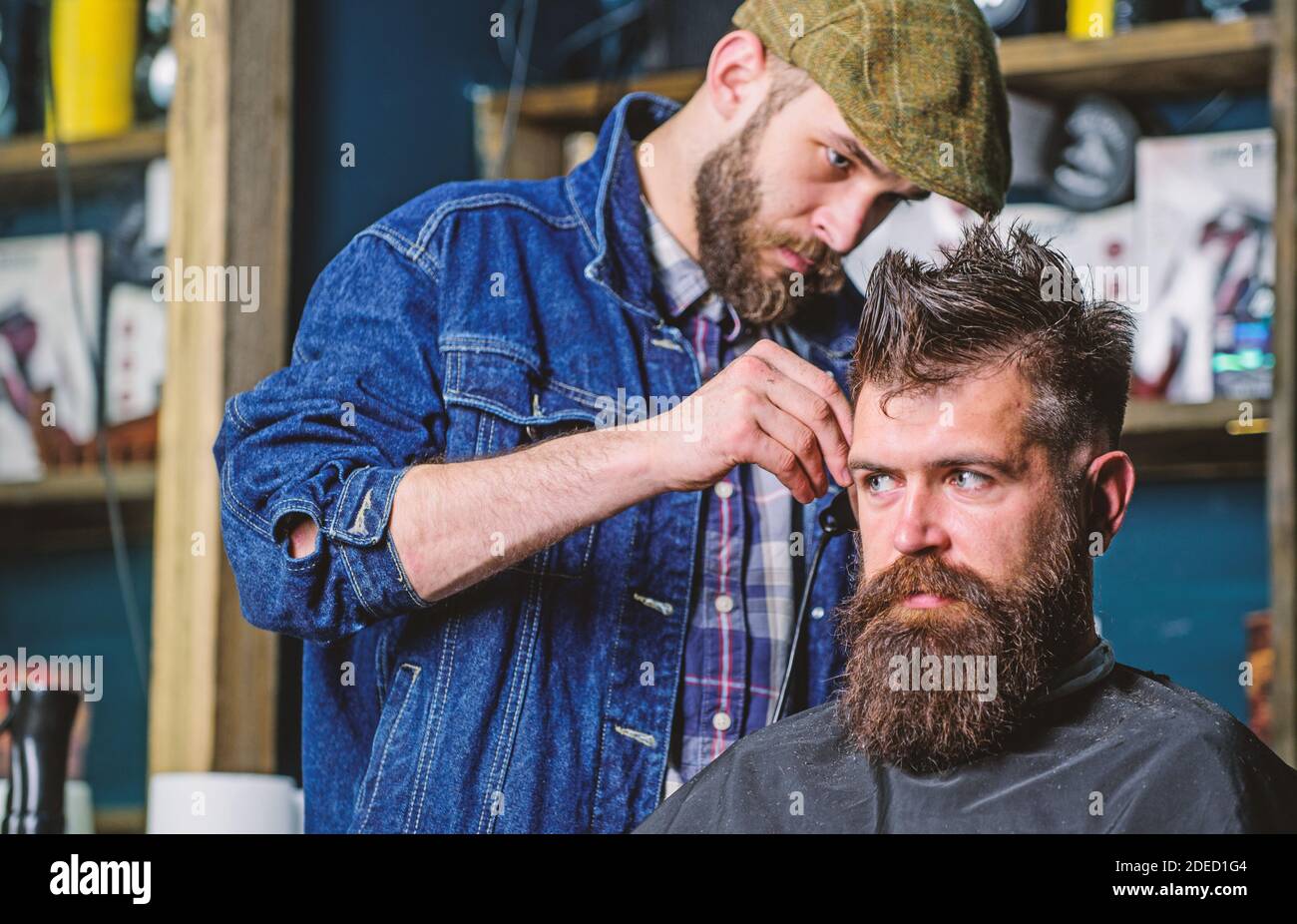 Barber in denim jacket busy with trimming hipster, barbershop ...