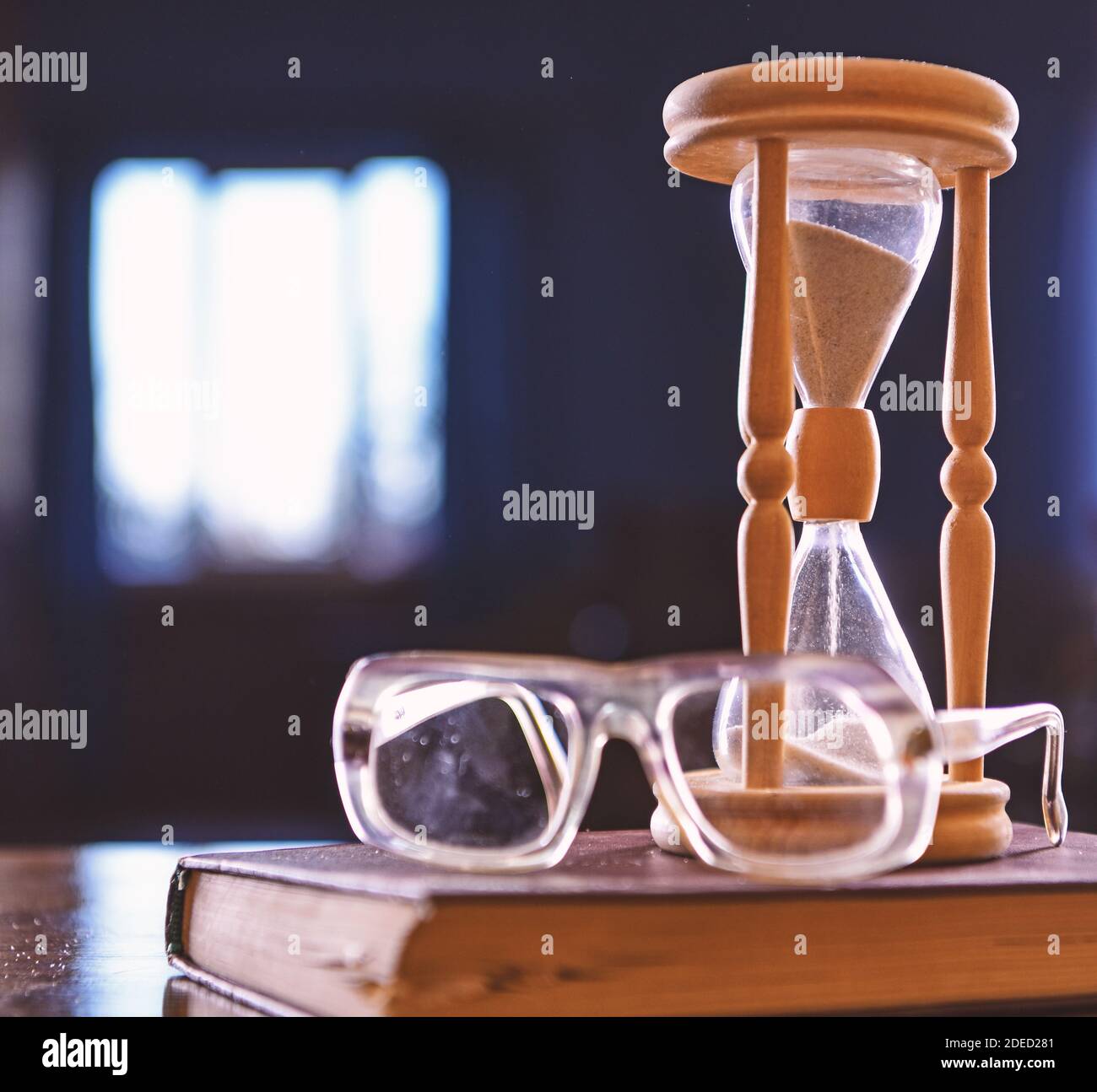 Hourglass, old book and eyeglasses on wooden table, dark background ...