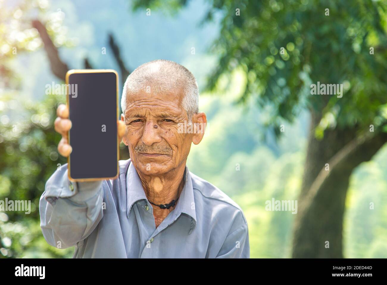 Rural farmer of Indian ethnicity holding mobile phone in his hand ...