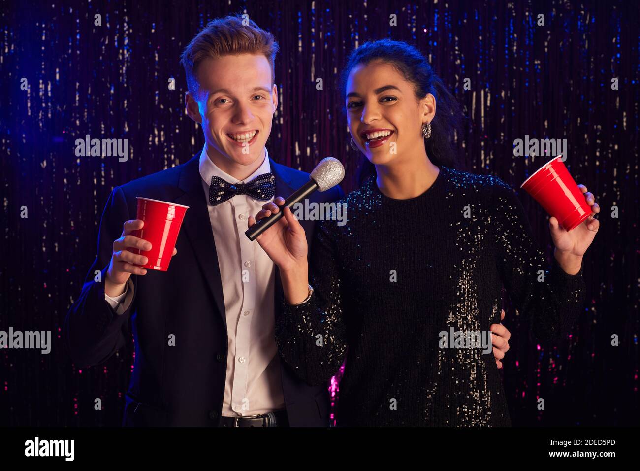 Waist up portrait of young couple holding microphone and smiling at ...