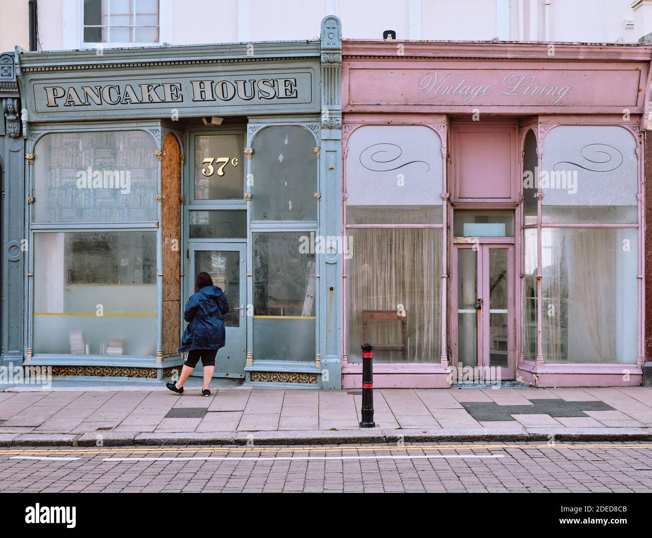 Empty closed old shopfronts and a passerby on a street in Hastings ...