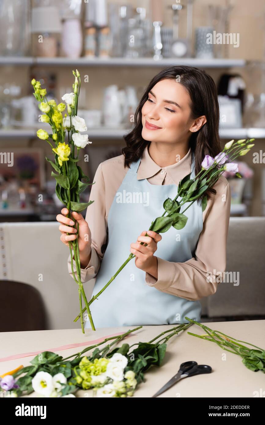 happy florist making bouquet with eustoma flowers near rack with vases ...