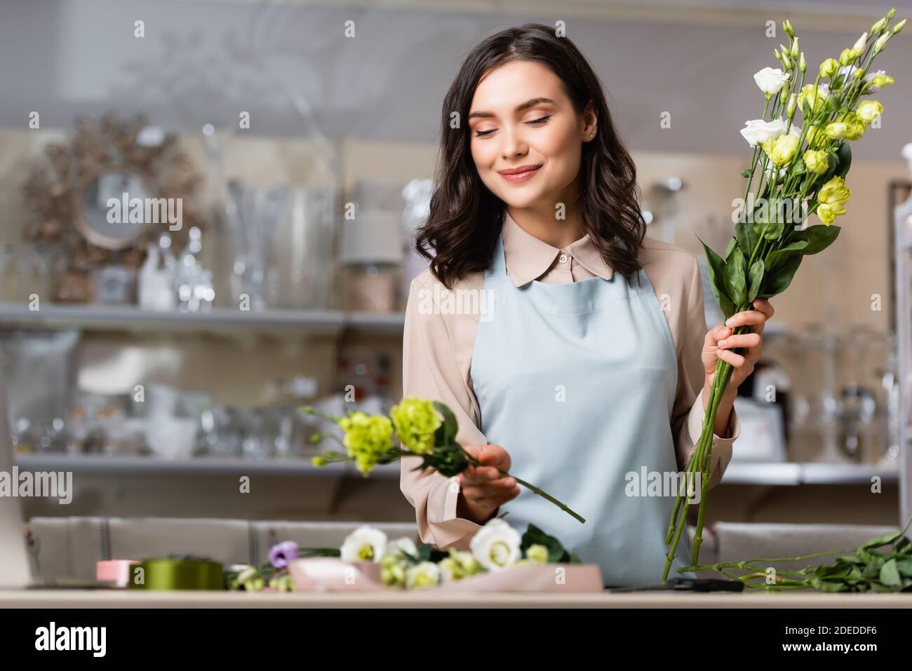 smiling florist in flower shop holding eustoma flowers while arranging ...