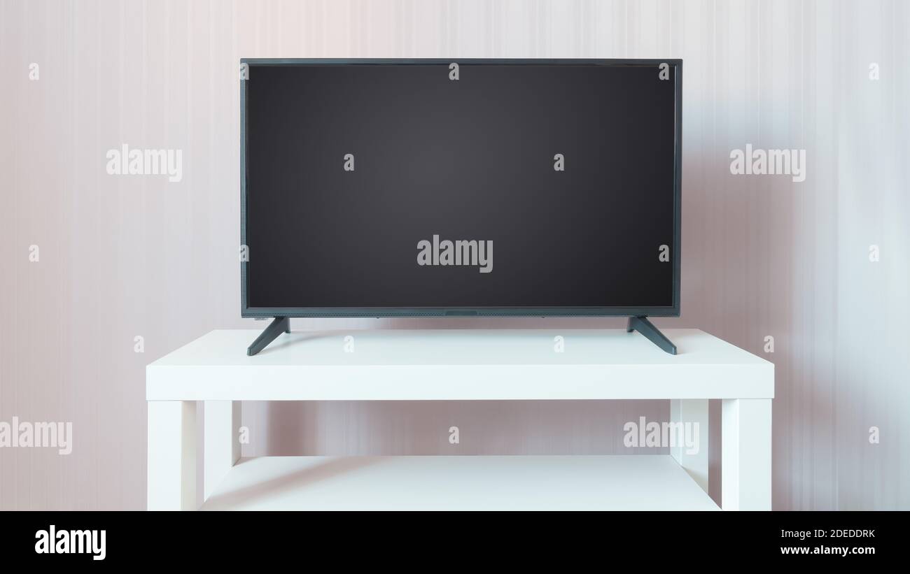 Black LCD TV with empty screen on a white stand against beige wall ...
