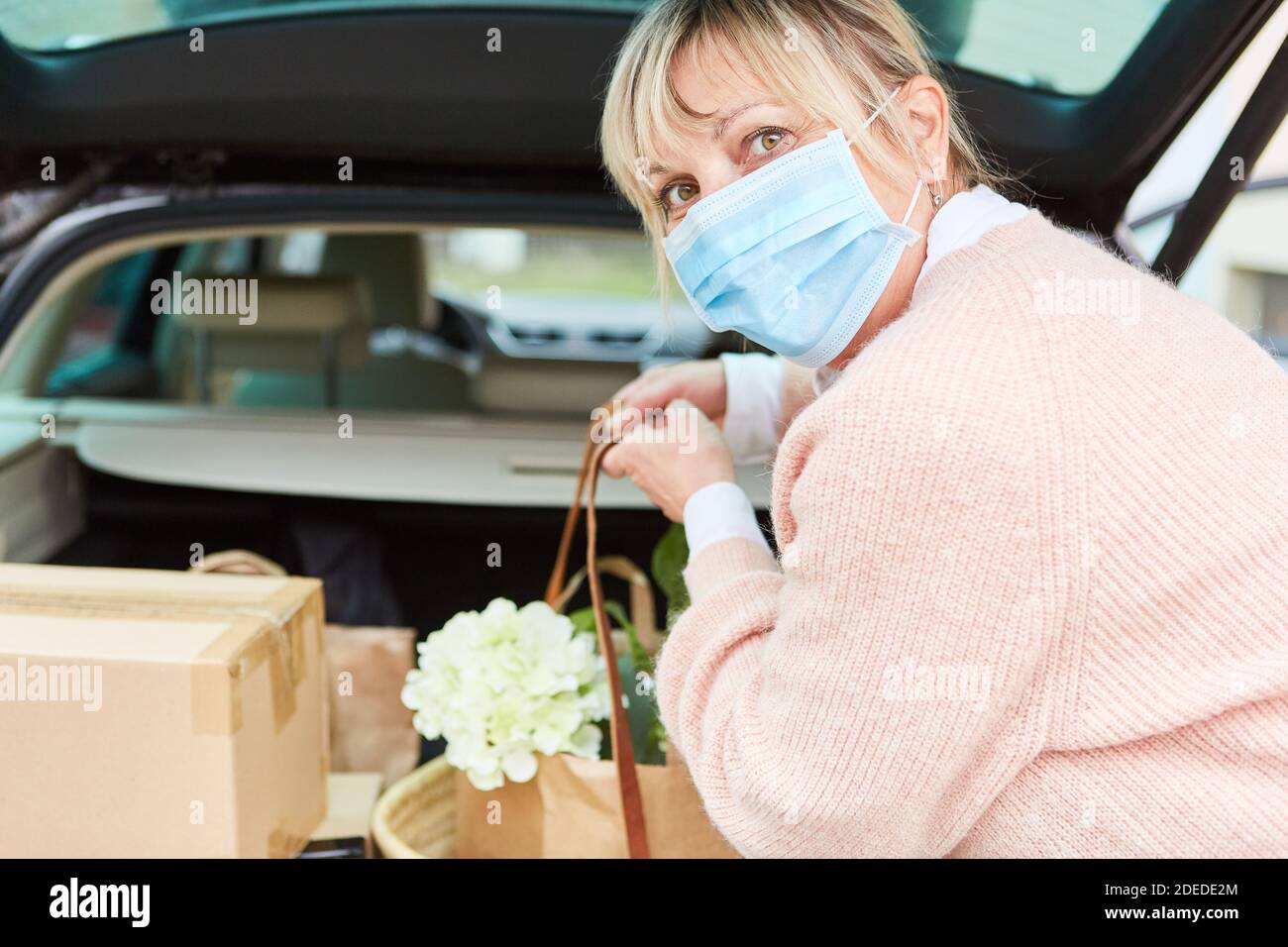 Woman with face mask has bag with purchases in her hands in front of a ...