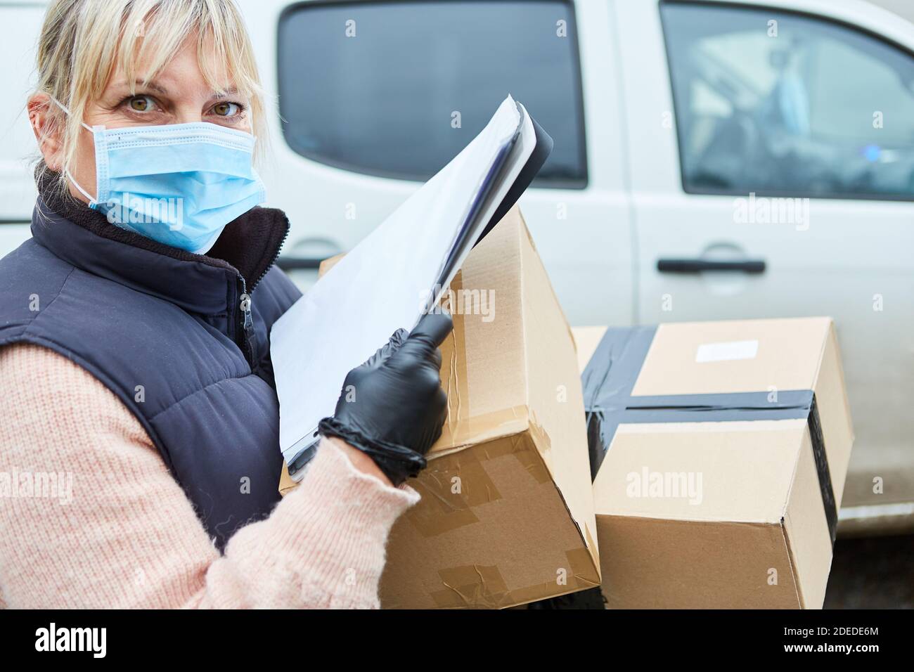 Parcel delivery woman with face mask checks delivery on list outside in ...