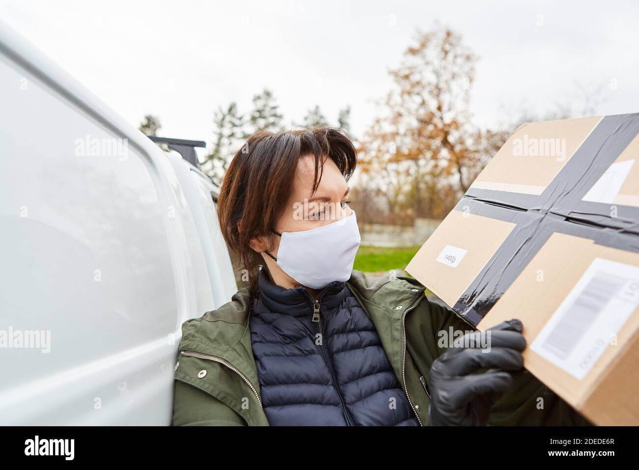 Delivery service parcel carrier with face mask is standing outside and ...