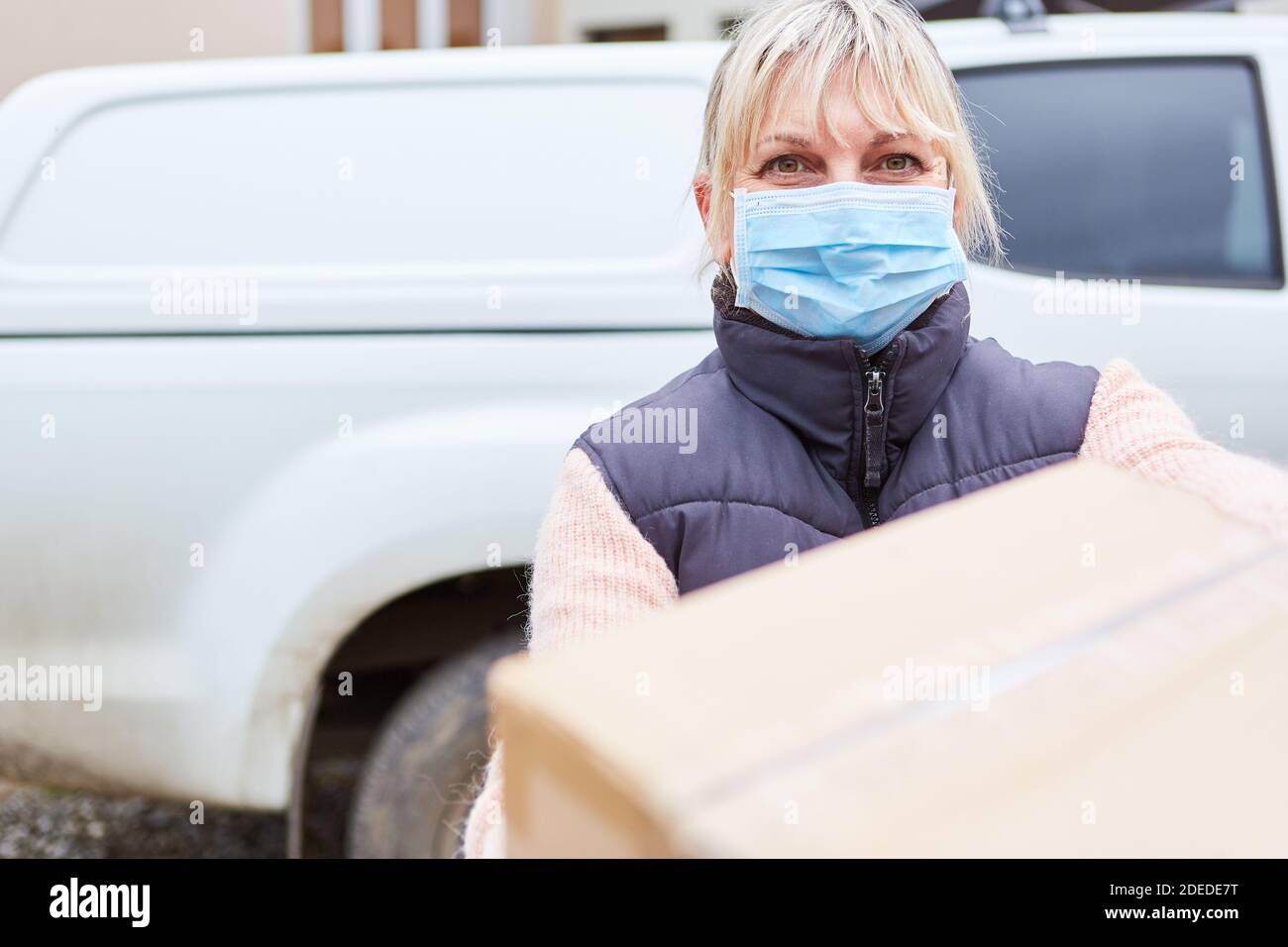 Parcel messenger with face mask outside in front of her vehicle ...