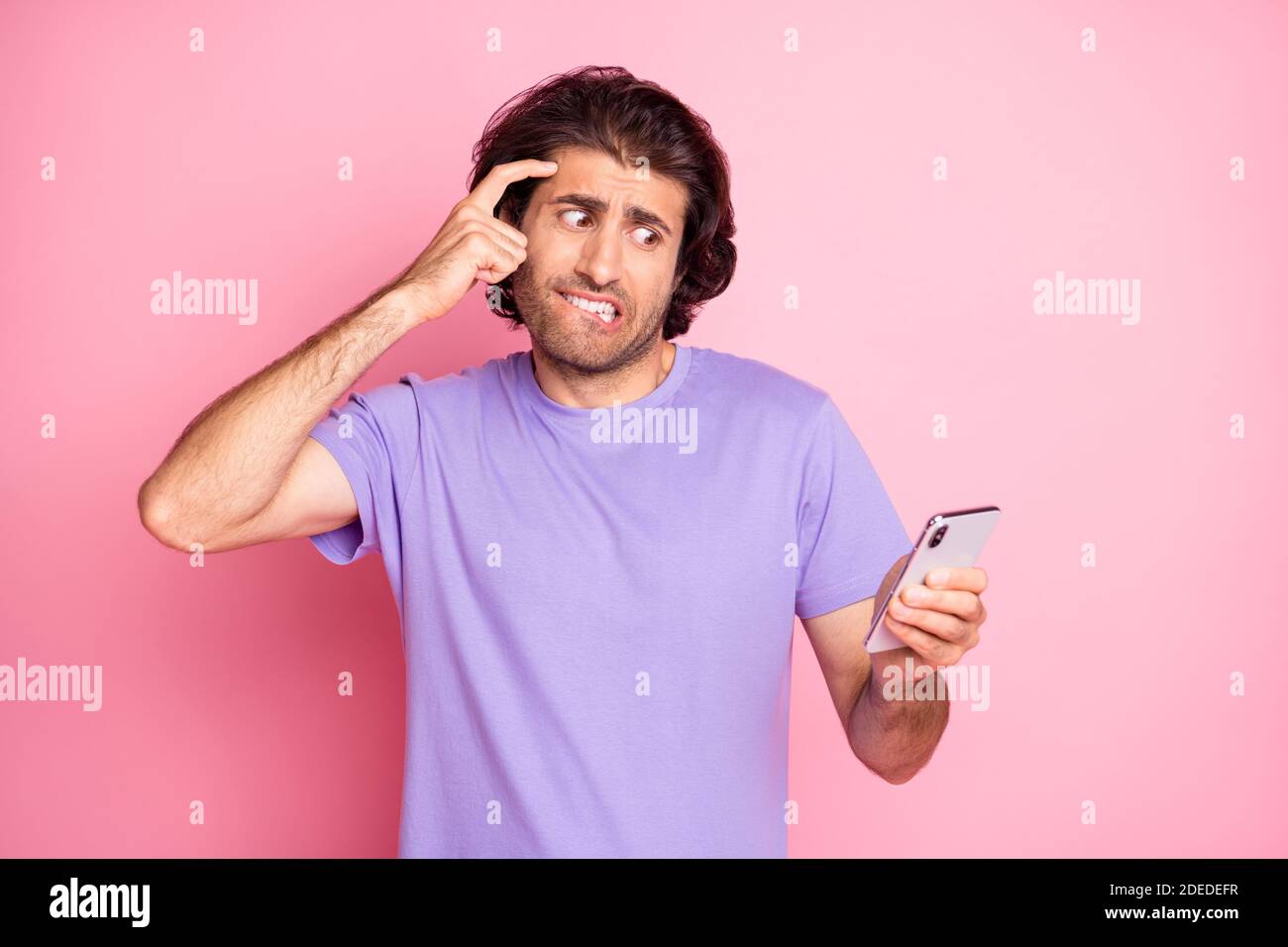Photo of handsome man scared loon phone hand on forehead bite lip ...