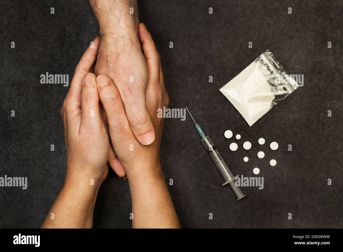 Woman hands holding the hand of an addicted man on a dark background ...