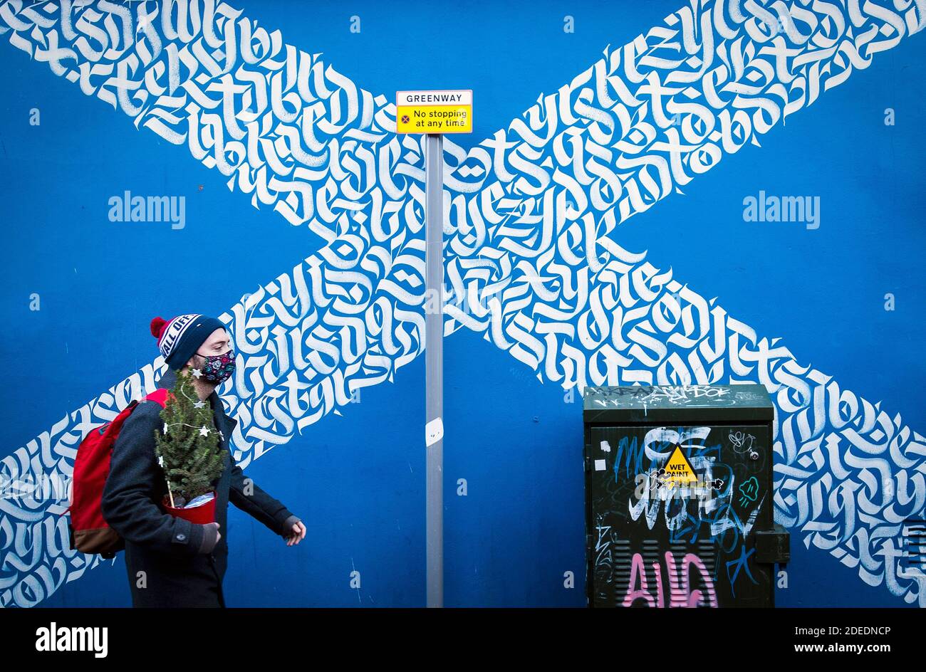 A man carrying a Christmas tree walks past a mural depicting a Saltire ...