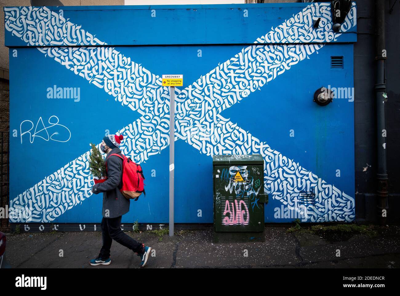 A man carrying a Christmas tree walks past a mural depicting a Saltire ...