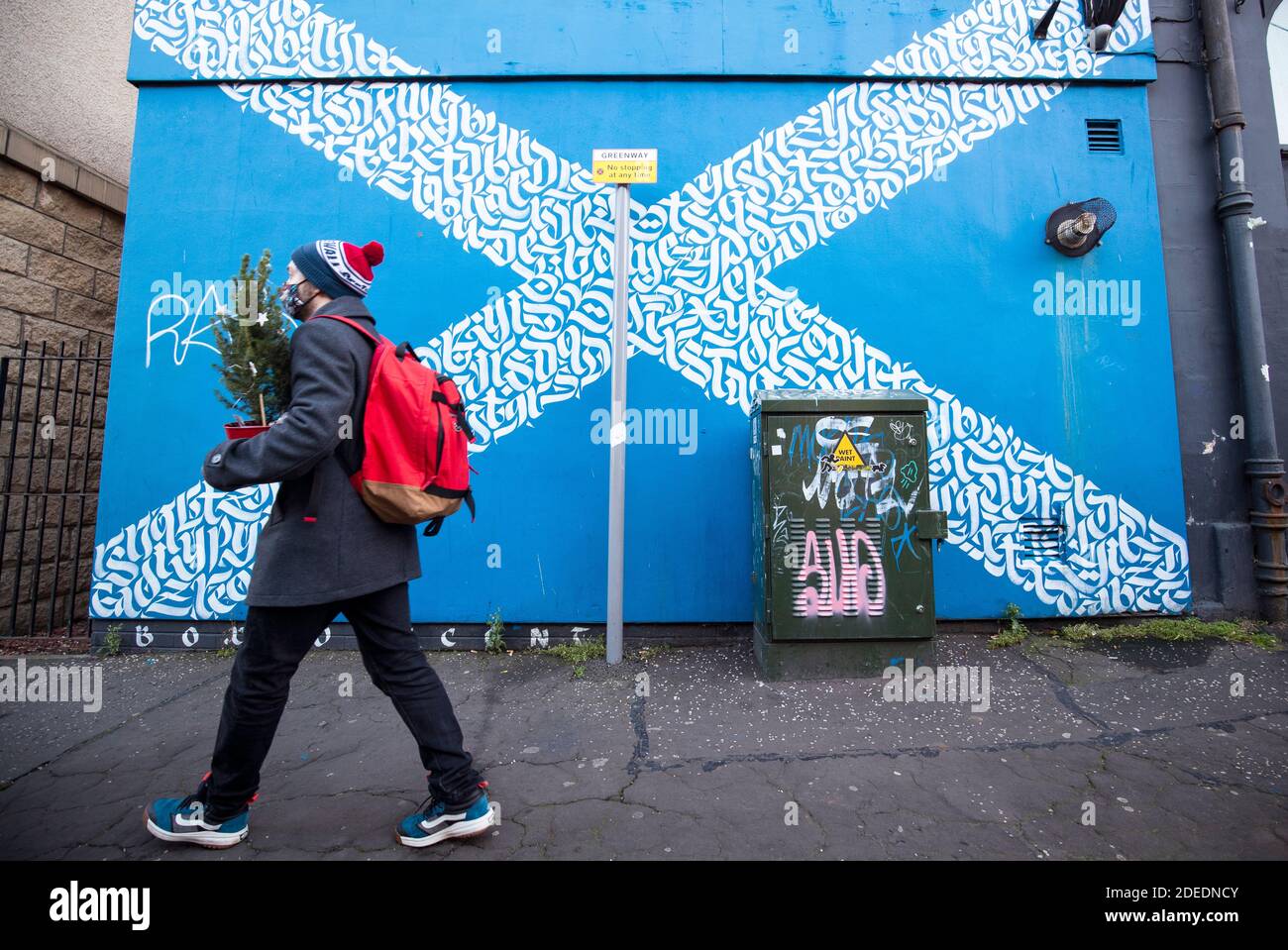 A man carrying a Christmas tree walks past a mural depicting a Saltire ...