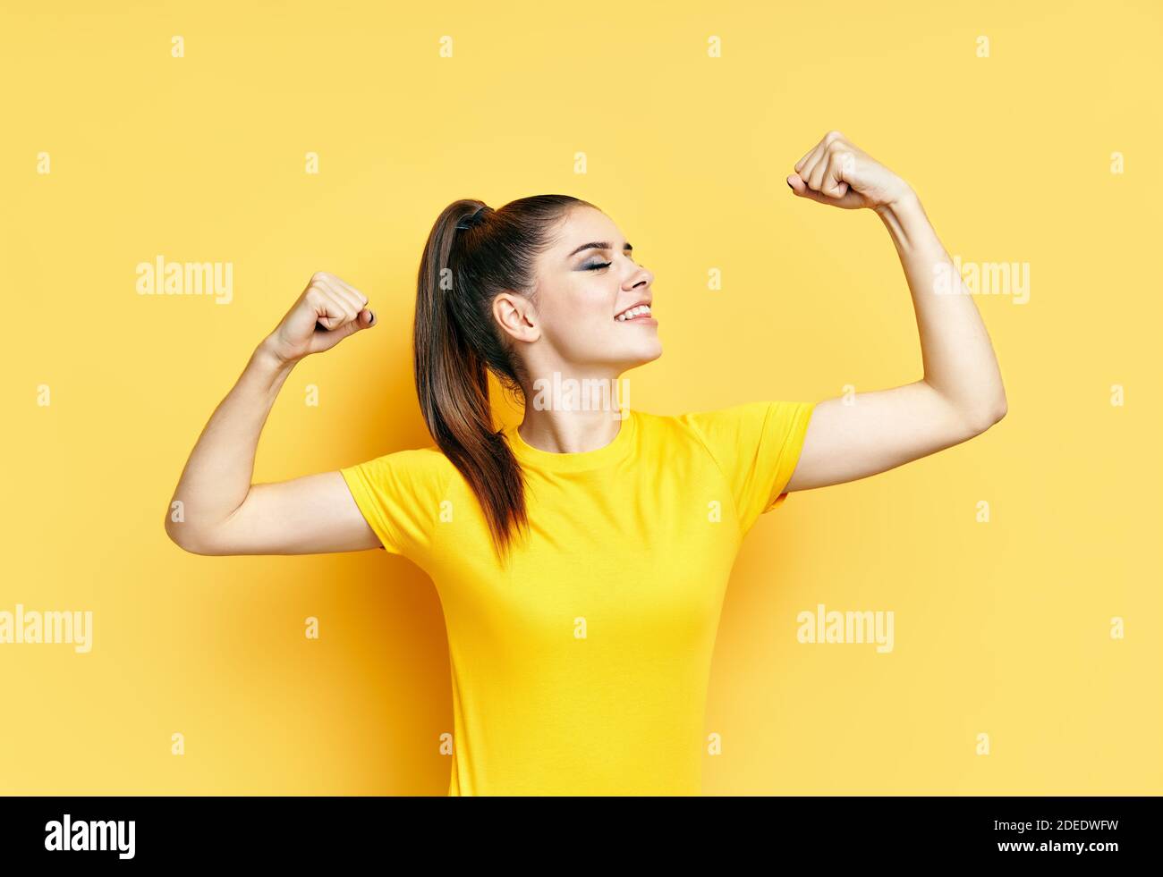 Powerful confident young woman showing arms muscles on yellow ...