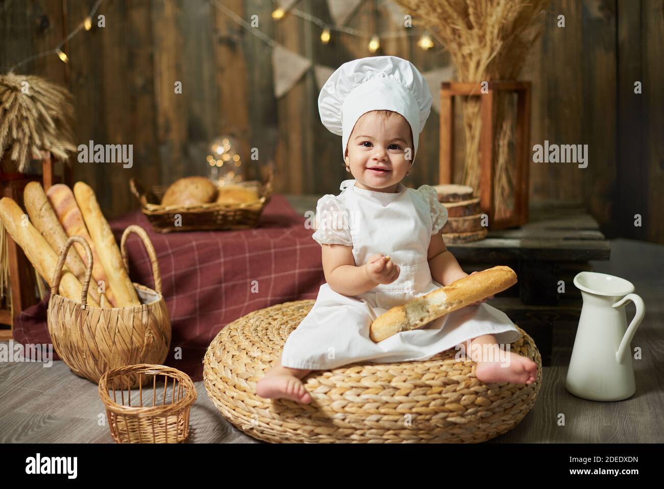 Adorable little baby baker with a French baguette in a rustic interior ...