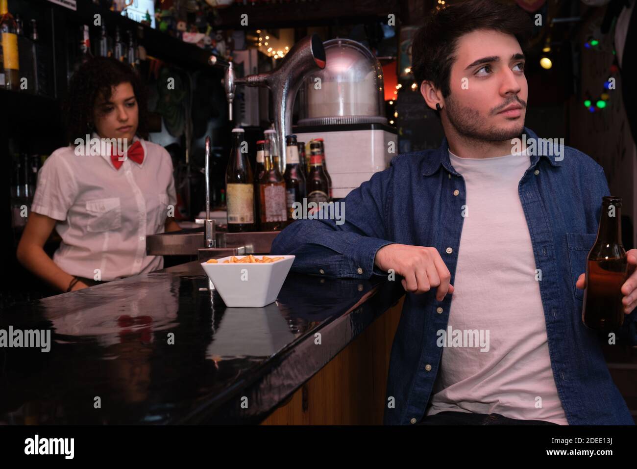 Young caucasian man with a beer bottle in his hand watching TV, football match in a bar ...