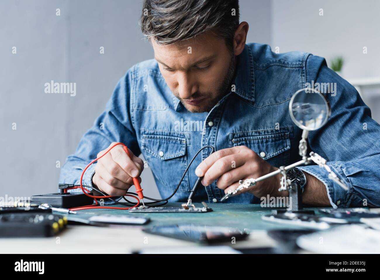 Focused repairman holding sensors of multimeter on disassembled part of ...