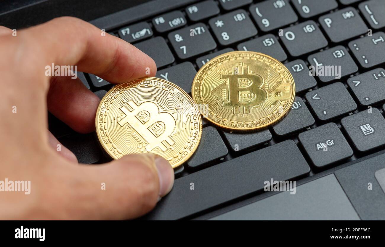 Hand placing two bitcoin gold coin symbols on a modern laptop keyboard ...