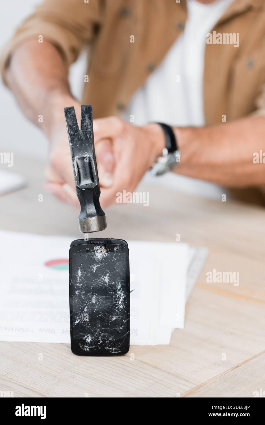 Cropped view of businessman holding hammer near smashed smartphone on ...