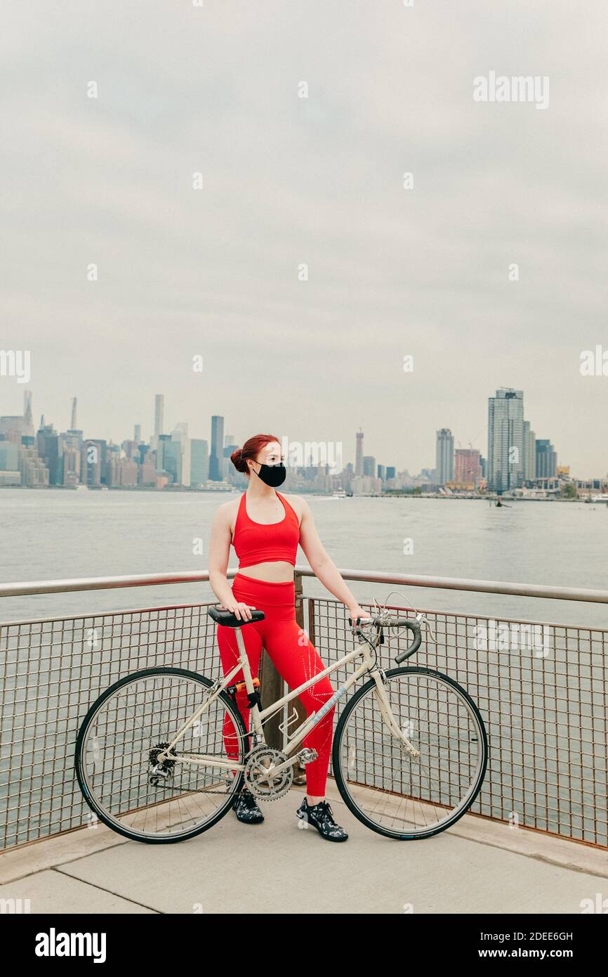 Young female cyclist wearing face mask with bike by waterfront Stock ...