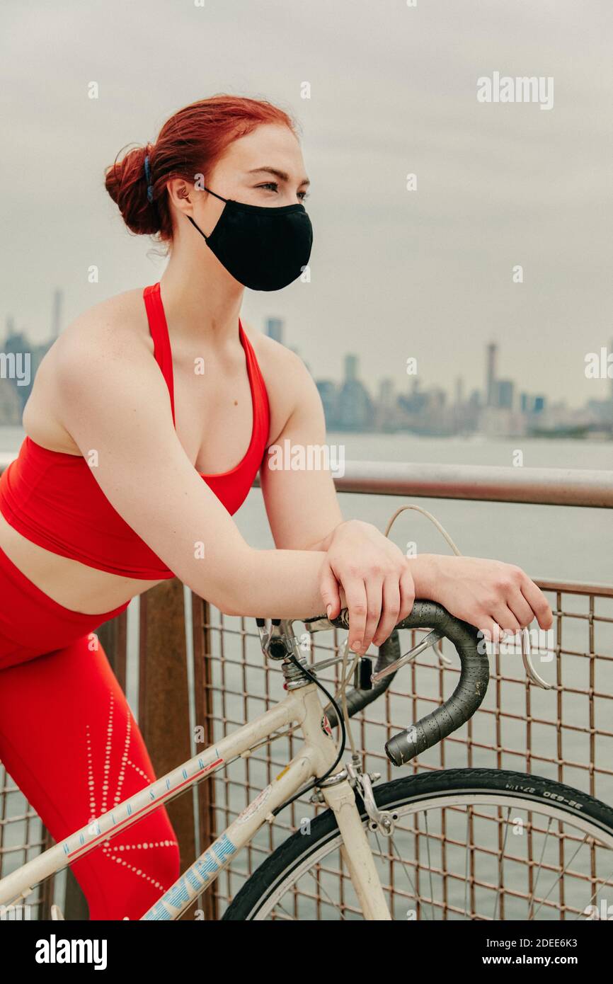 Young female cyclist wearing face mask with bike by waterfront Stock ...