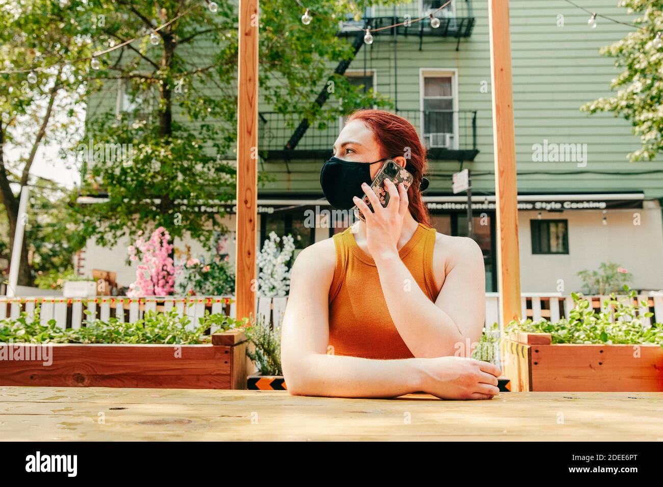 Young woman sitting in an outdoor restaurant table, wearing face mask ...