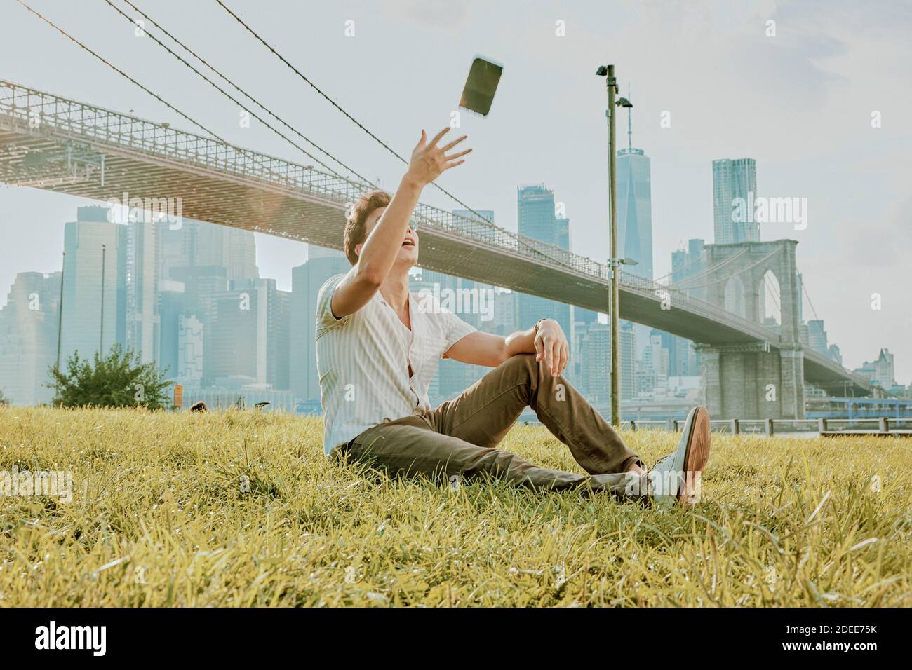 Young man sitting outdoors in park throwing phone mid air Stock Photo ...
