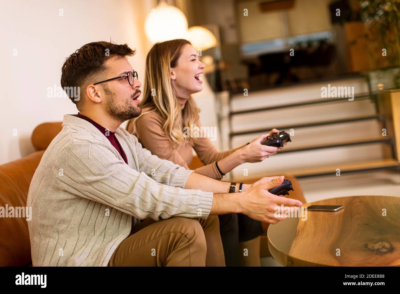 Handsome young couple playing video games at home, sitting on sofa and ...