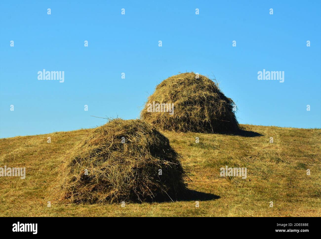 A view of two haystacks on the hilltop with a clear blue sky background ...