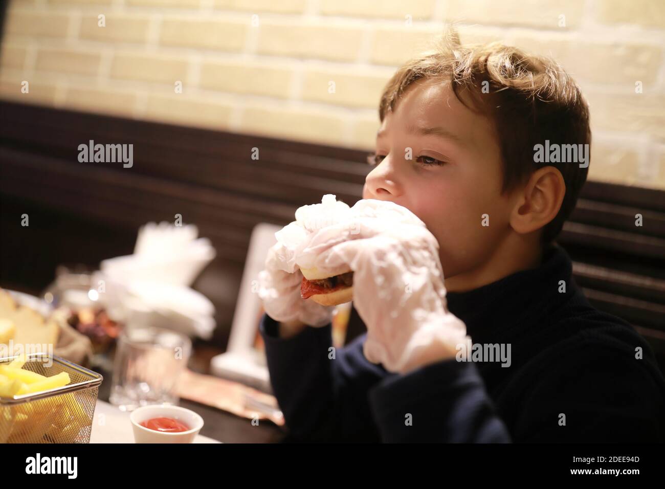 Child with gloves eating burger in restaurant Stock Photo - Alamy